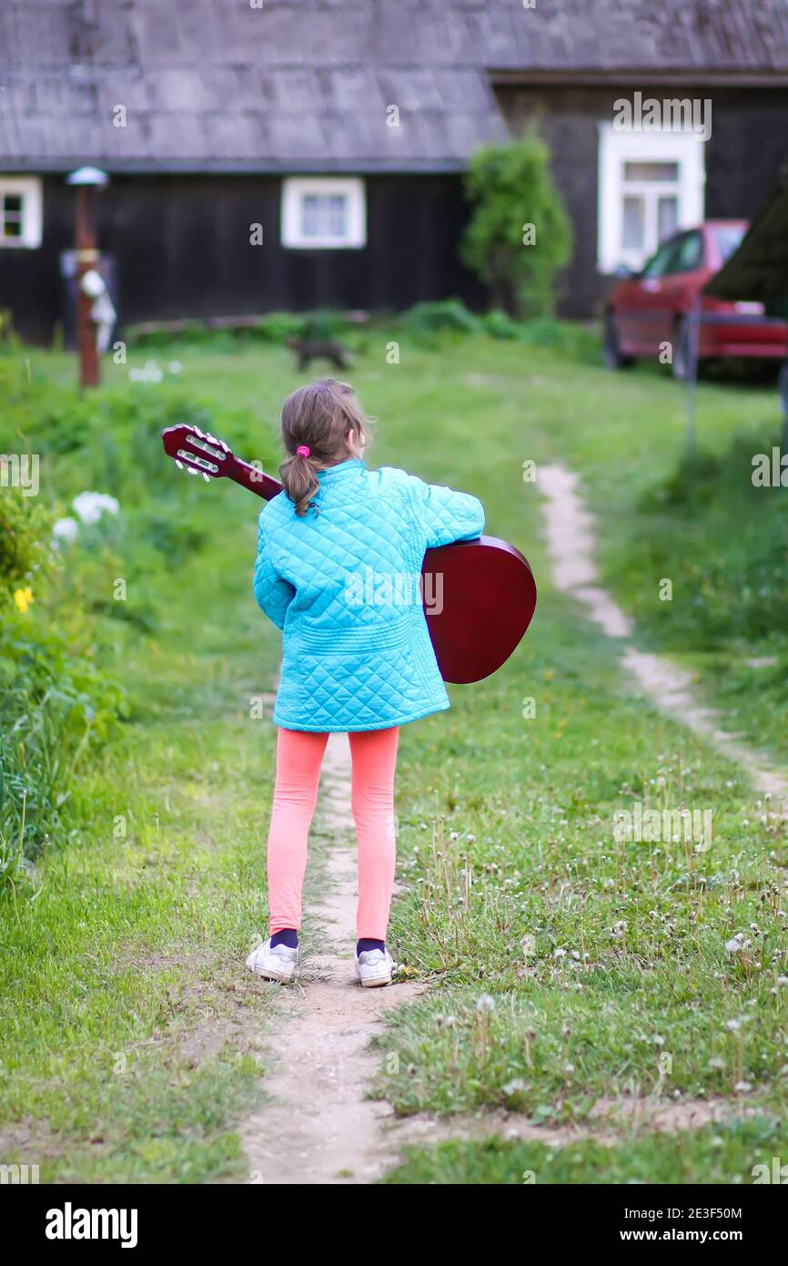 Little girl playing guitar and singing outdoors on green meadow at ...