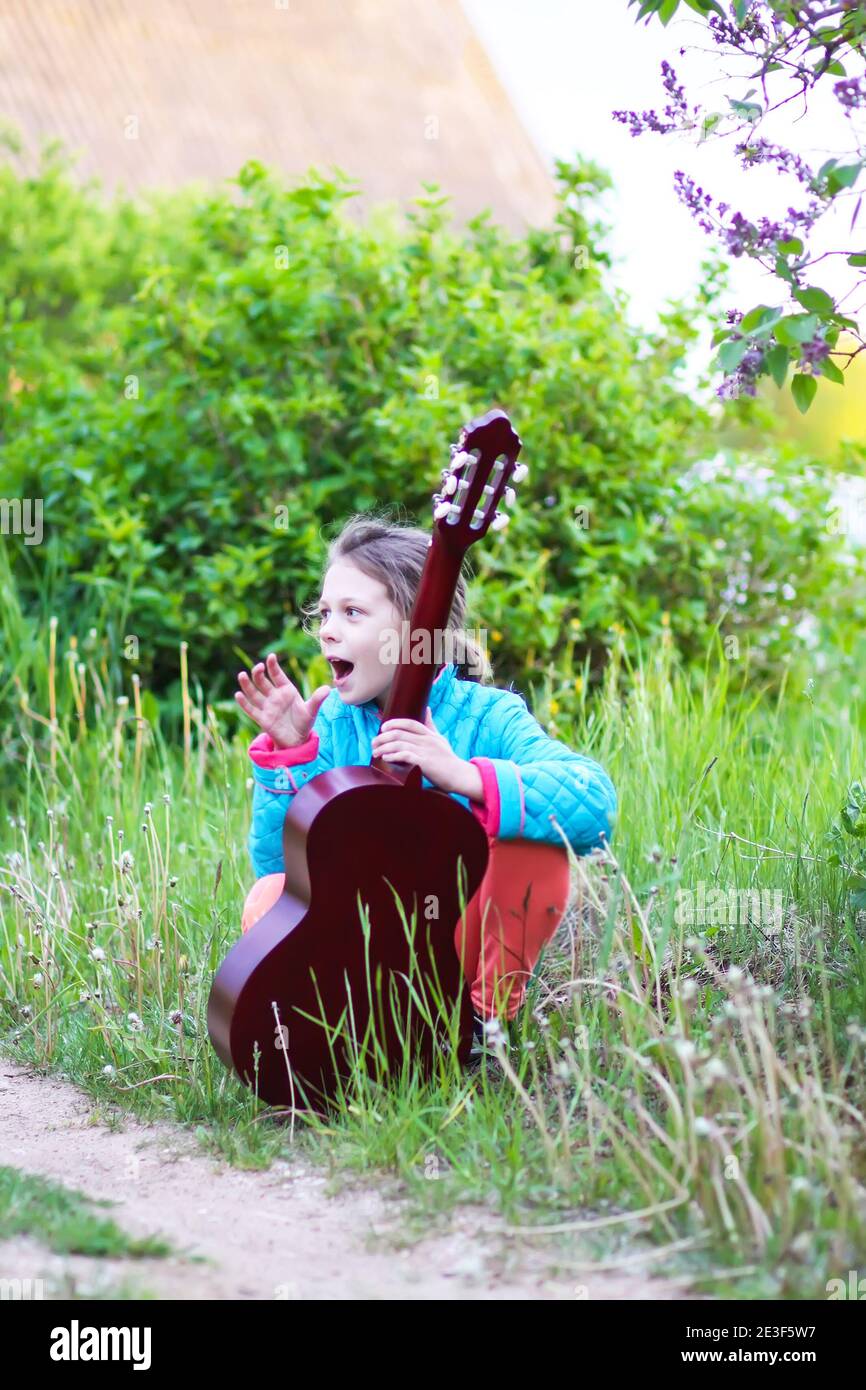 Little girl playing guitar and singing outdoors on green meadow at ...
