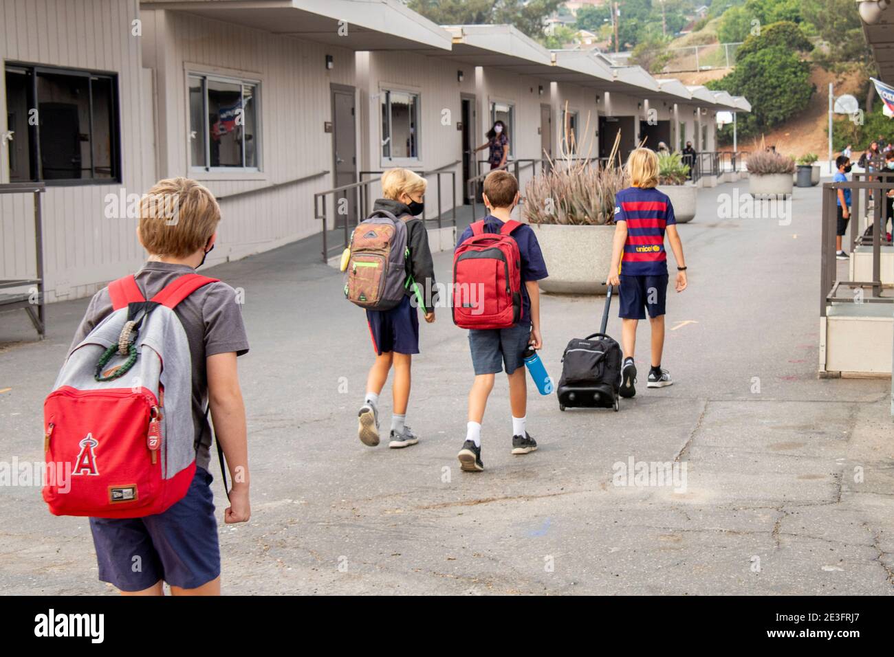 Carrying or wheeling their backpacks, four teen boys arrive at the ...