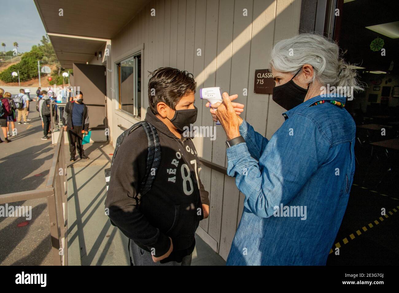 Wearing a safety face mask and using a digital thermometer, a ...