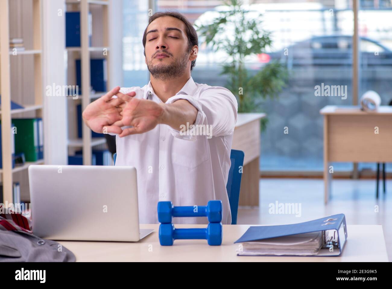 Young employee doing sport exercises at workplace Stock Photo - Alamy