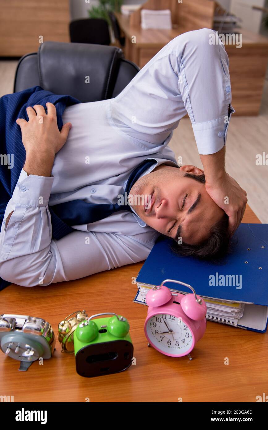 Young businessman sleeping in the office in time management concept ...