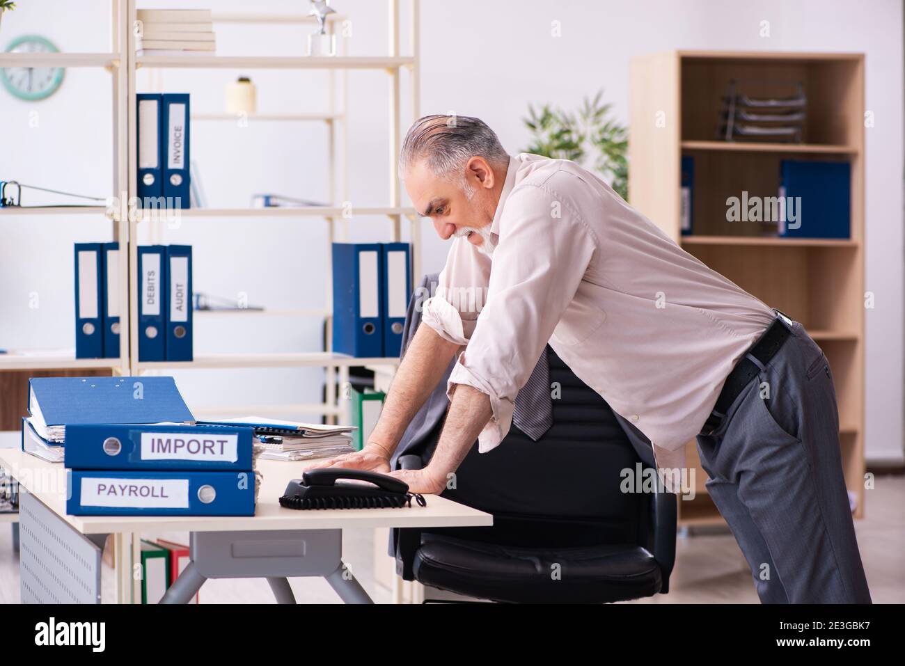 Senior male employee doing physical exercises at workplace Stock Photo ...