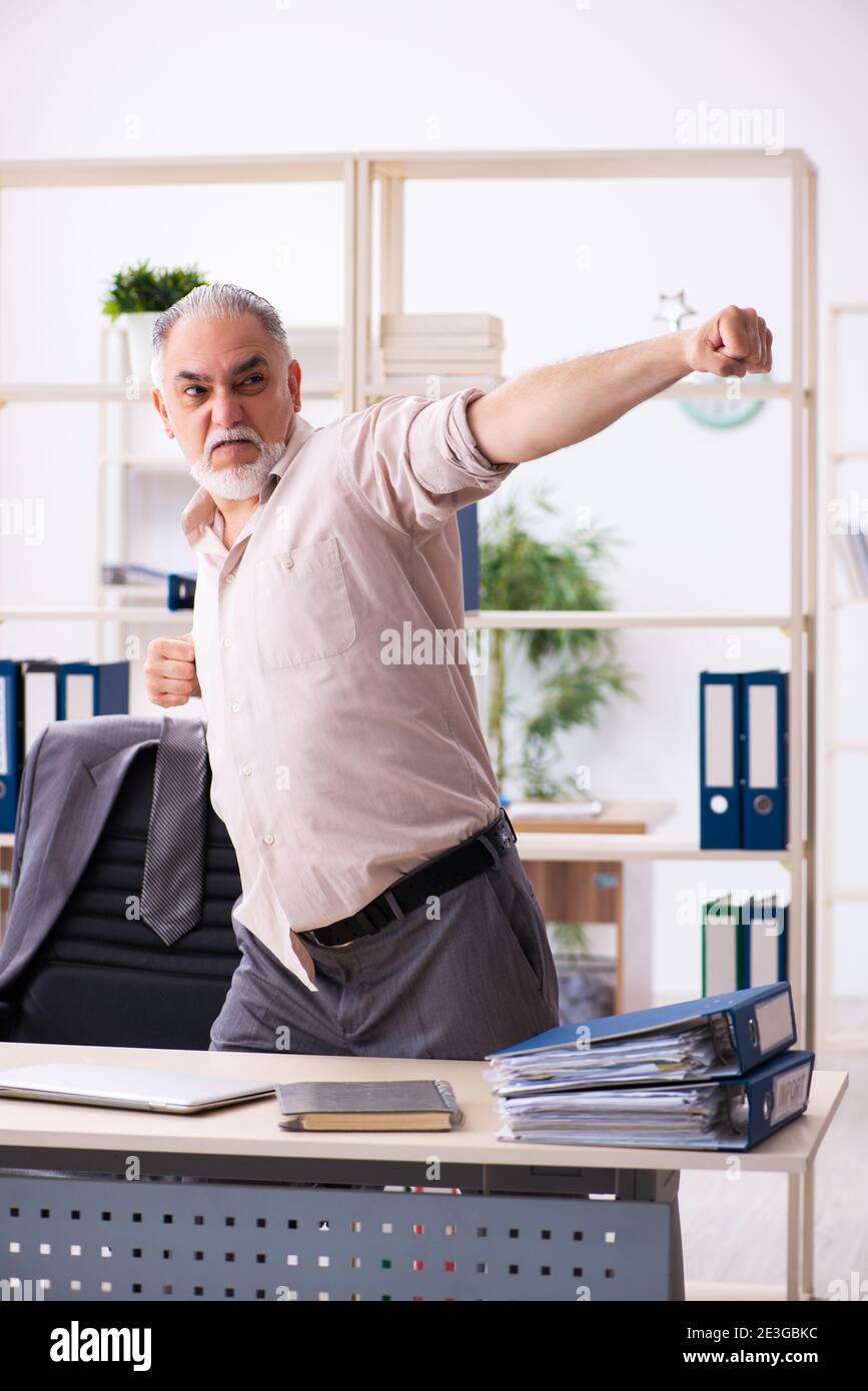 Senior male employee doing physical exercises at workplace Stock Photo ...