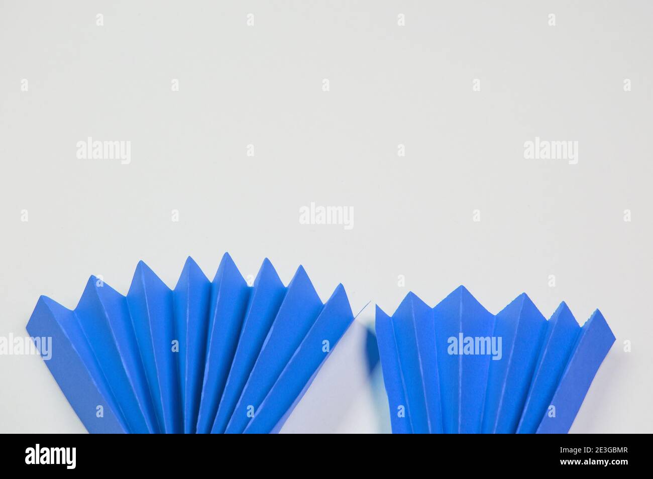 Two blue origami paper fans located on the bottom edge on a white ...