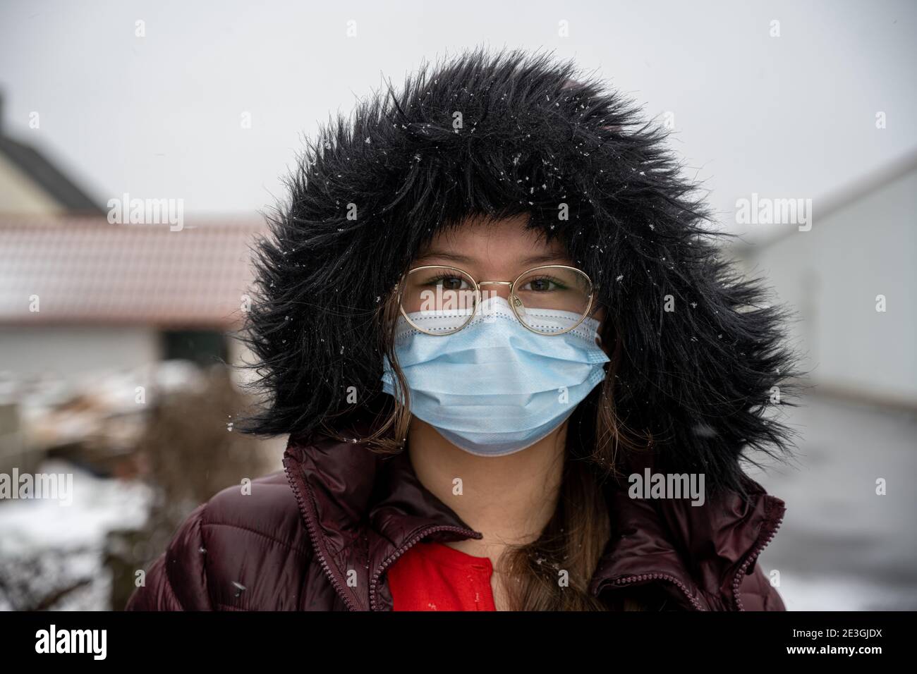 A teenage girl with in a winter jacket with a hood wearing a protective ...