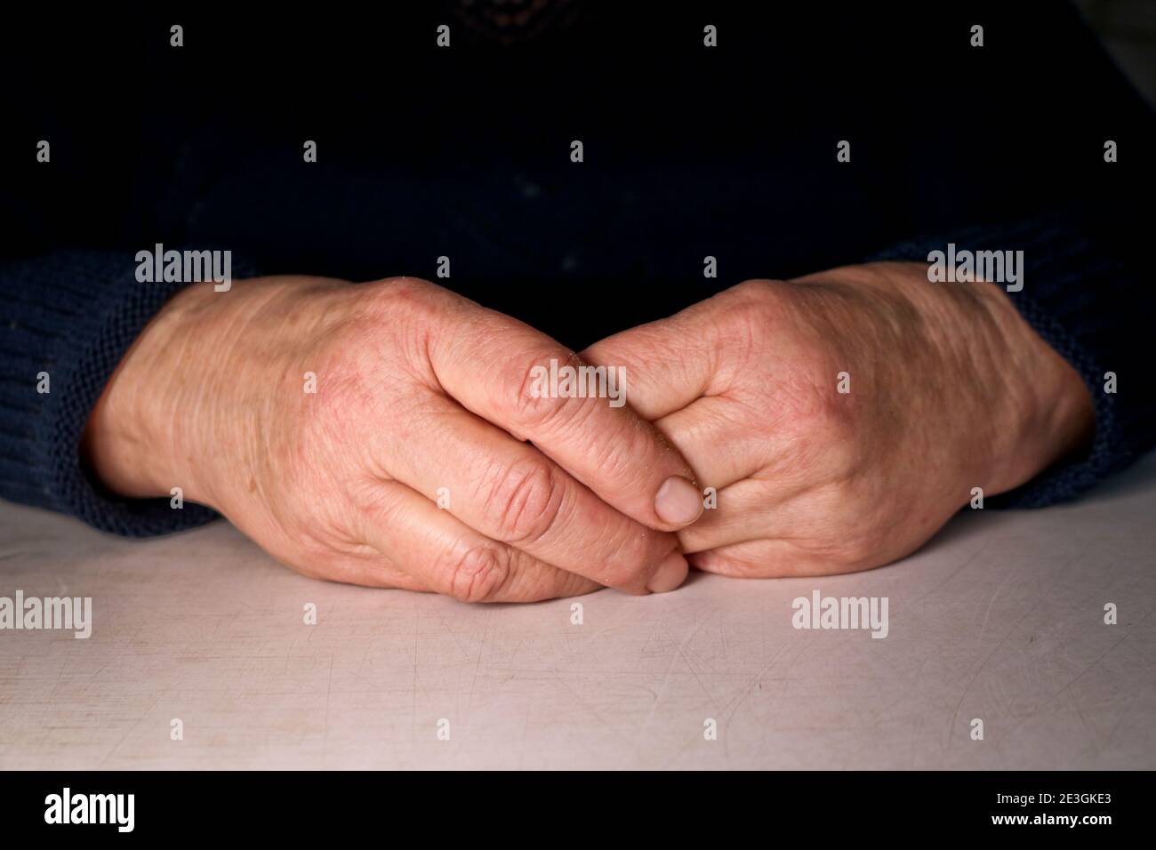 The old woman's clasped hands lie on the table. Wrinkles on the hands ...