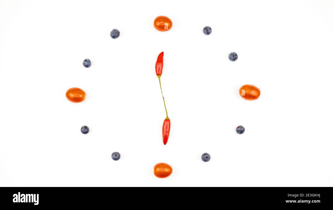 A clock from cherry tomatoes, blueberries and red chillies on a white ...