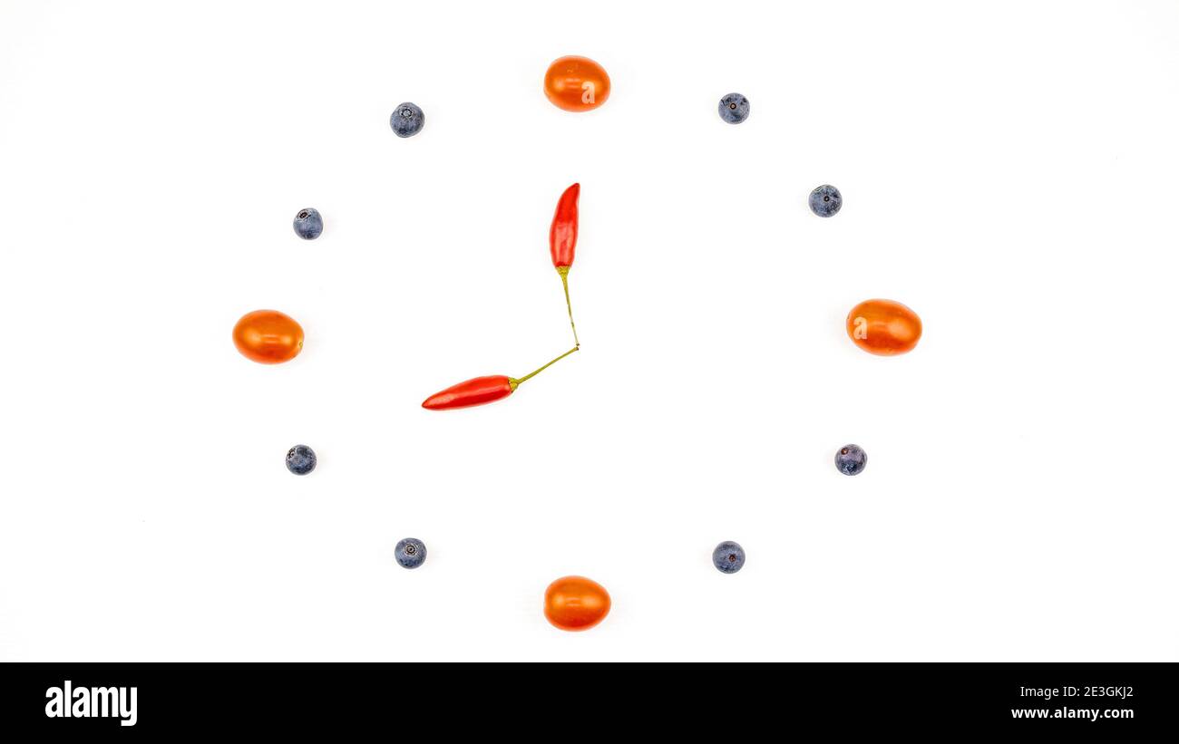 A clock from cherry tomatoes, blueberries and red chillies on a white ...