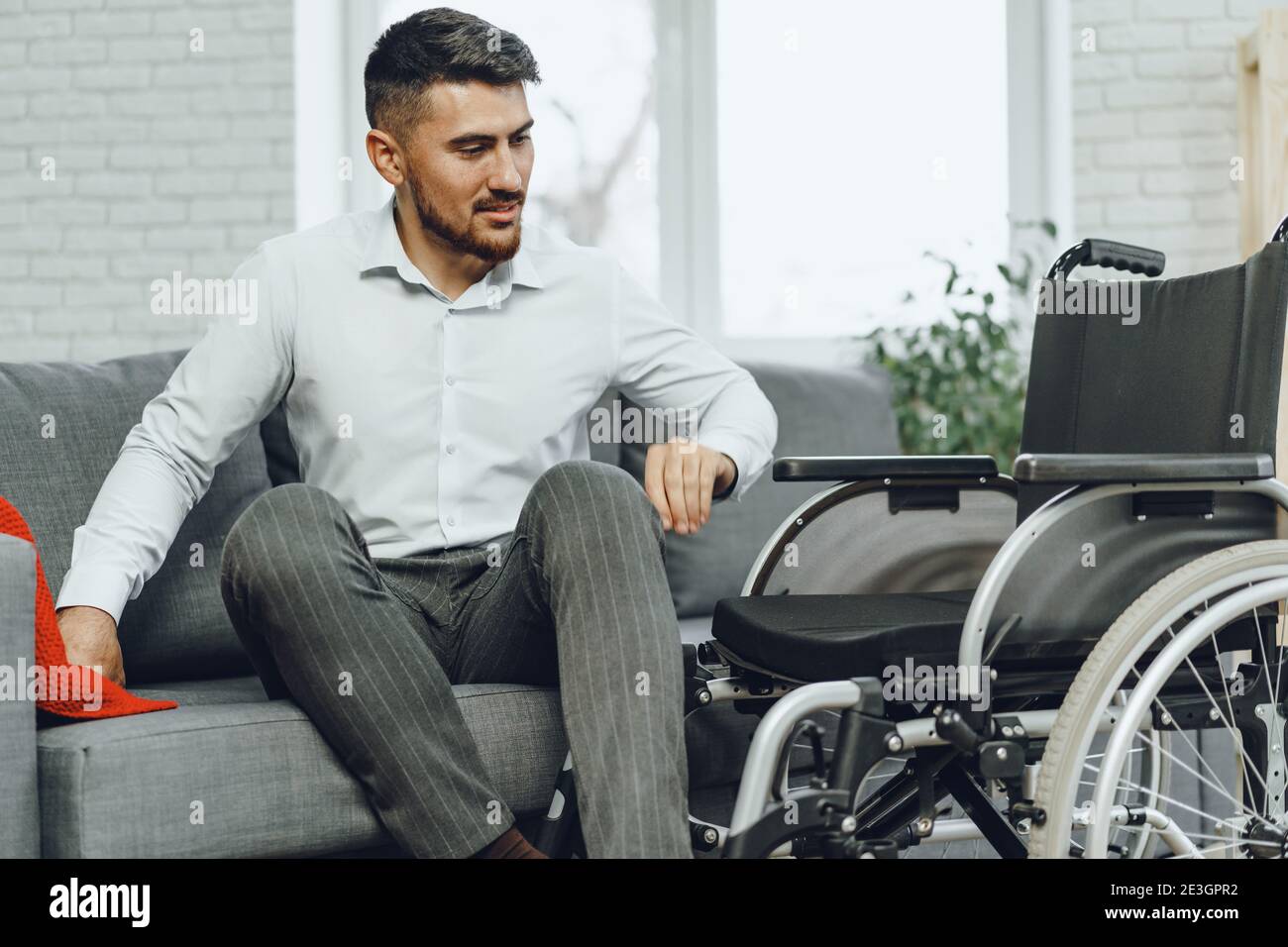 Disabled man tries to sit down on a sofa from wheelchair Stock Photo ...