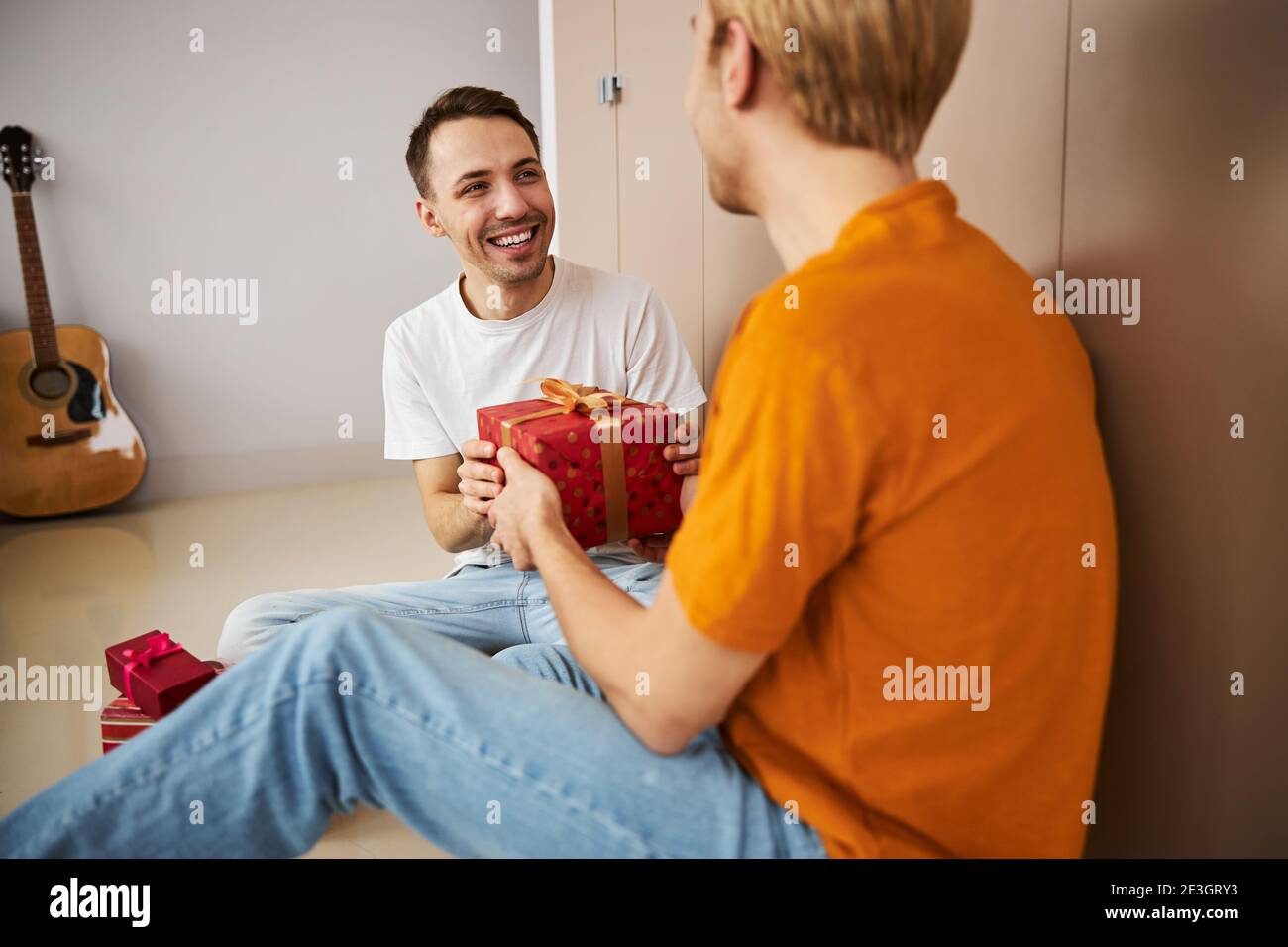 Loving young man giving present to joyful boyfriend Stock Photo - Alamy