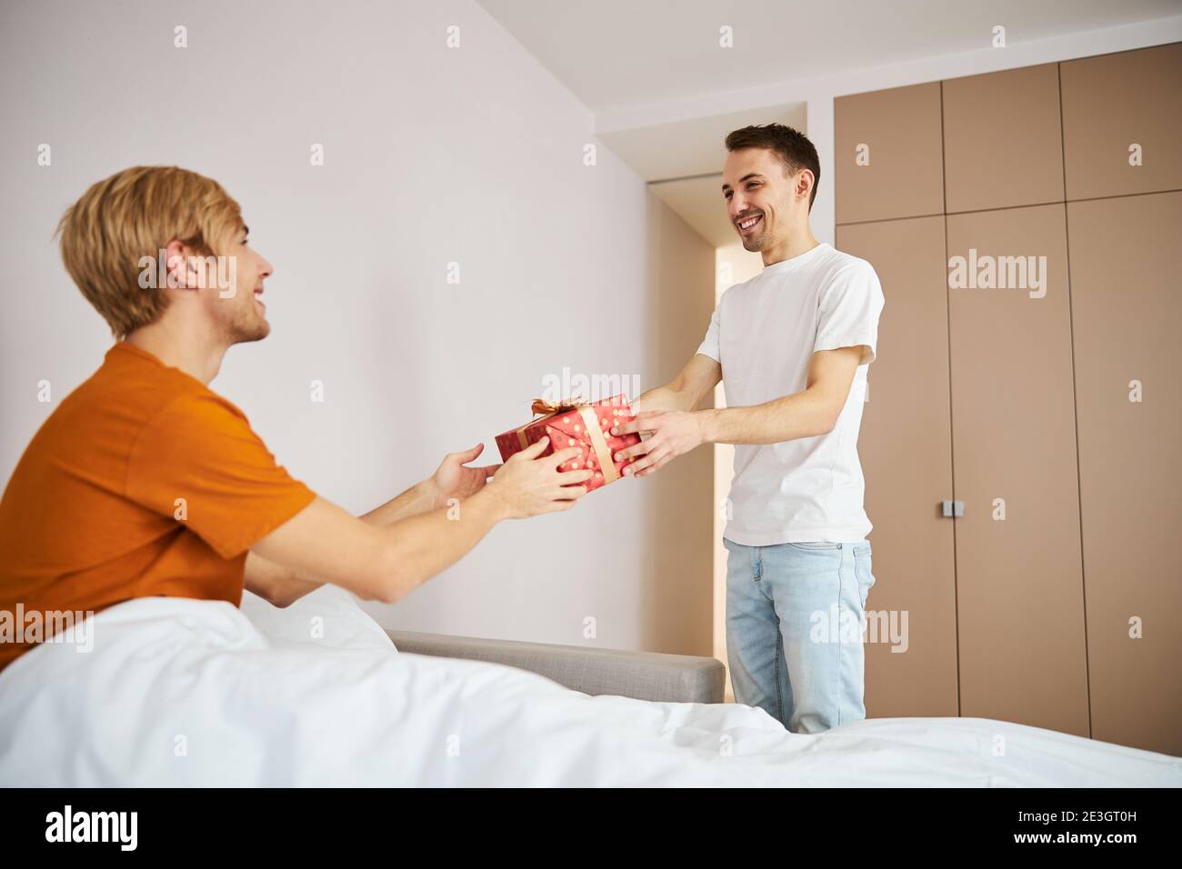 Joyful young man giving present to his boyfriend at home Stock Photo ...