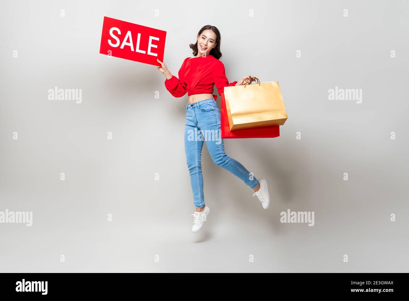 Happy Asian woman holding shopping bags and red sale sign jumping in ...