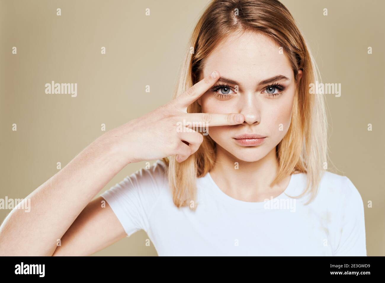 Cheerful blonde woman in a white T-shirt gestures with her hand emotions beige background Stock ...