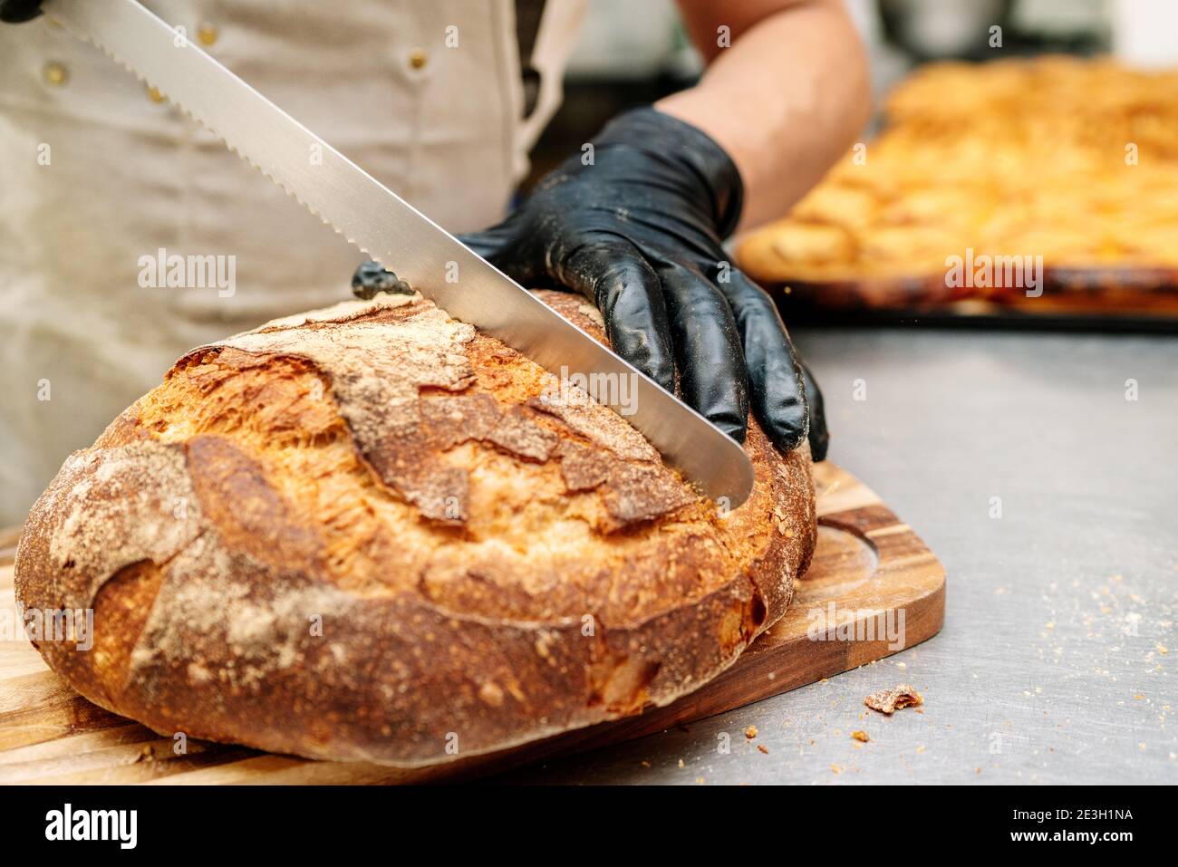 selective focus of hand of baker cutting a loaf of bread with a knife ...