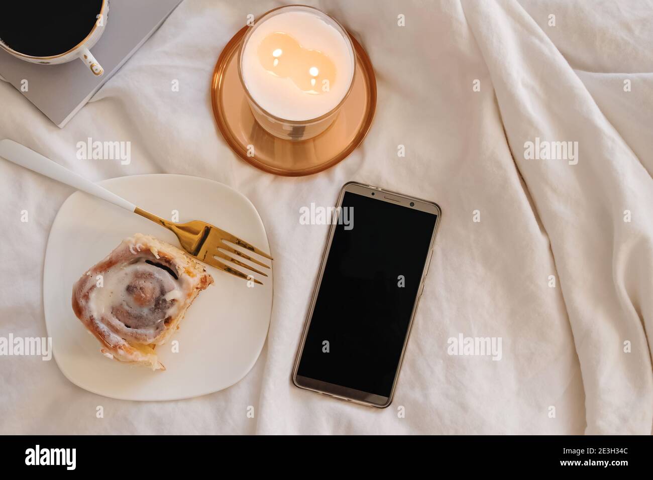 Smartphone with empty screen on the bed with cinnamon bun and burning ...