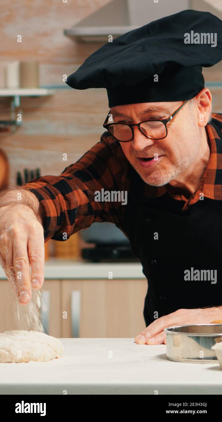 Bakery man sieving flour over dough on table in home kitchen. Retired ...