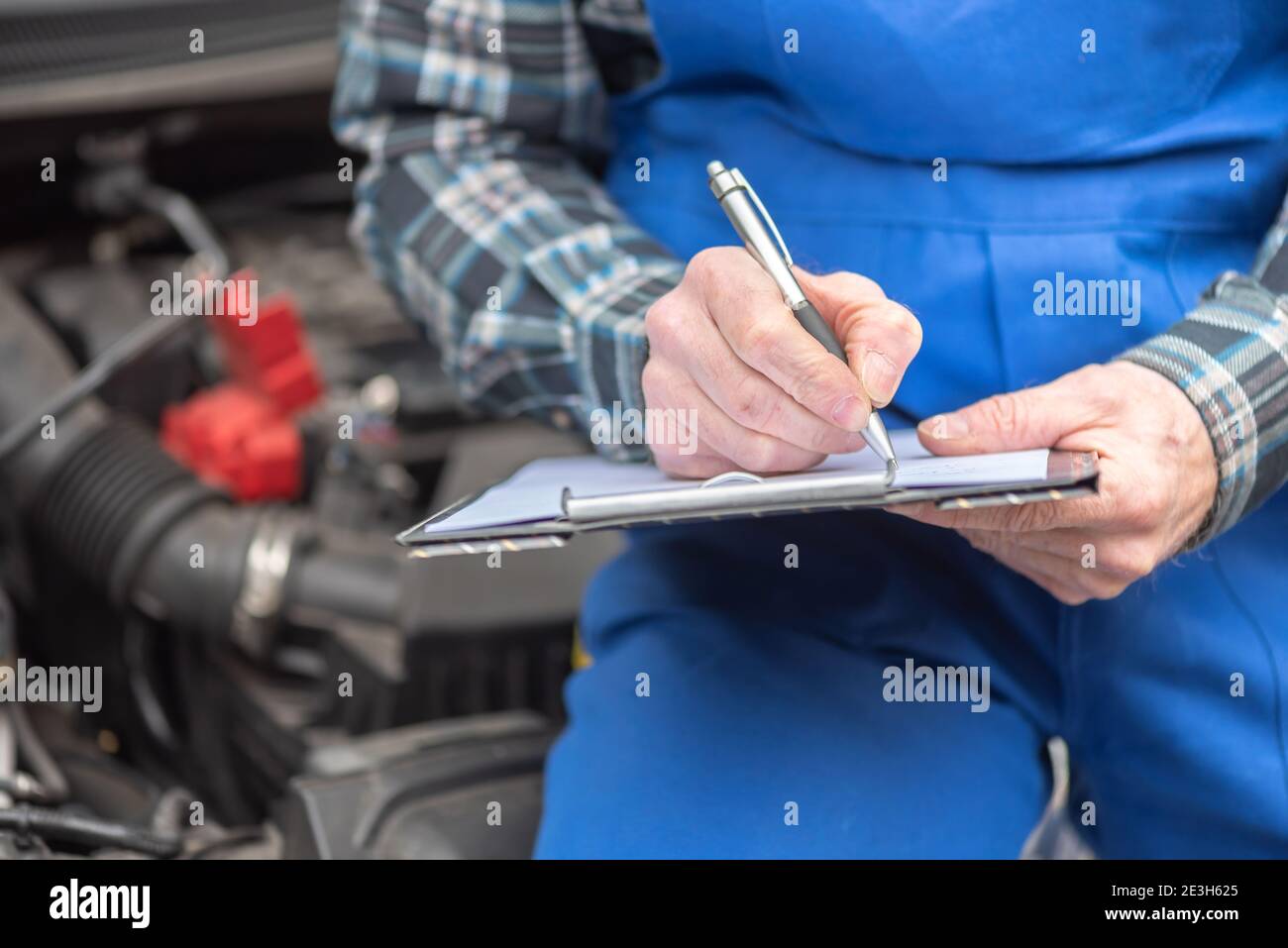 Car mechanic checking a car engine and writing on clipboard Stock Photo ...