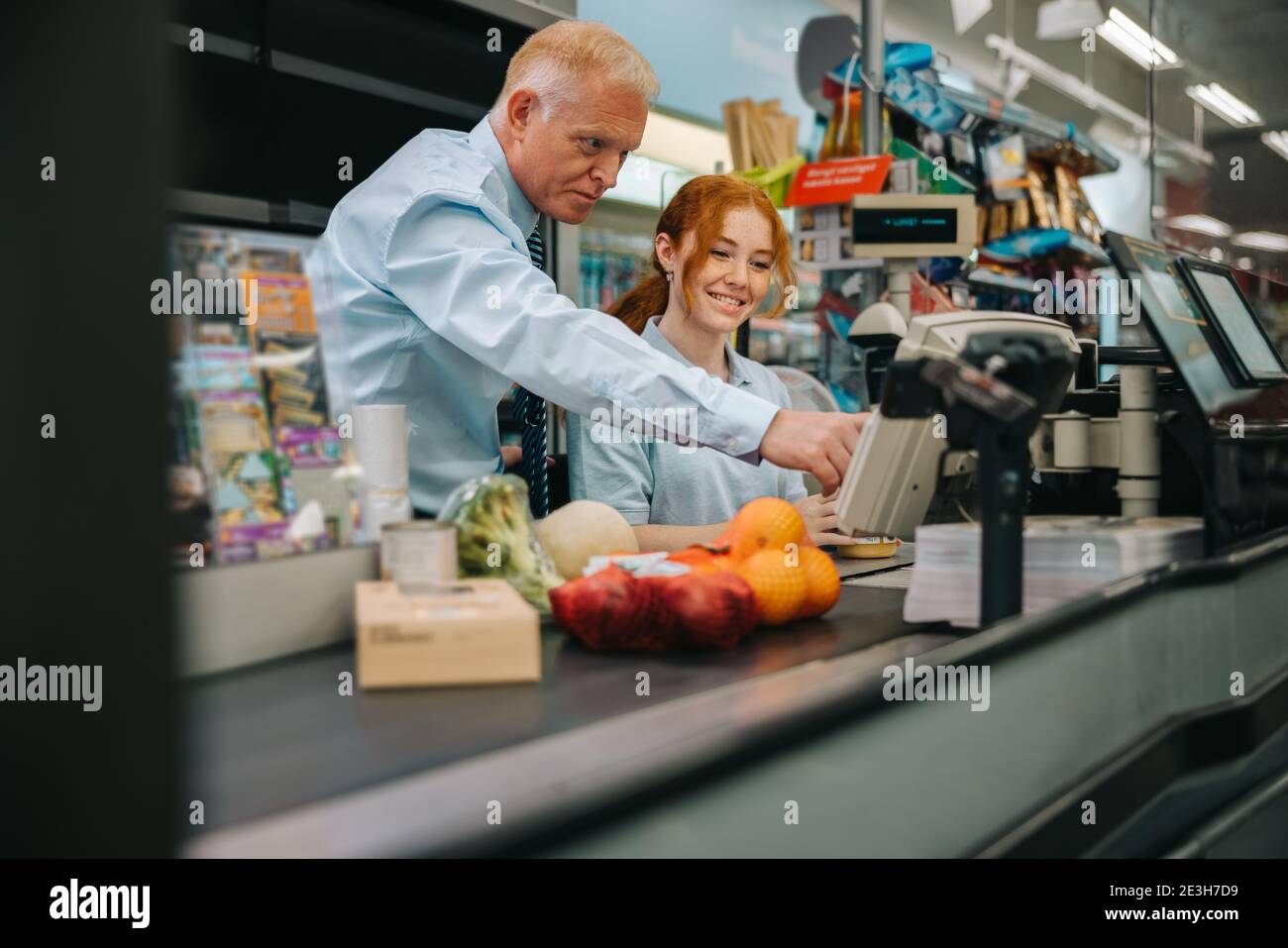 Senior manager helping new employee at checkout counter in supermarket ...