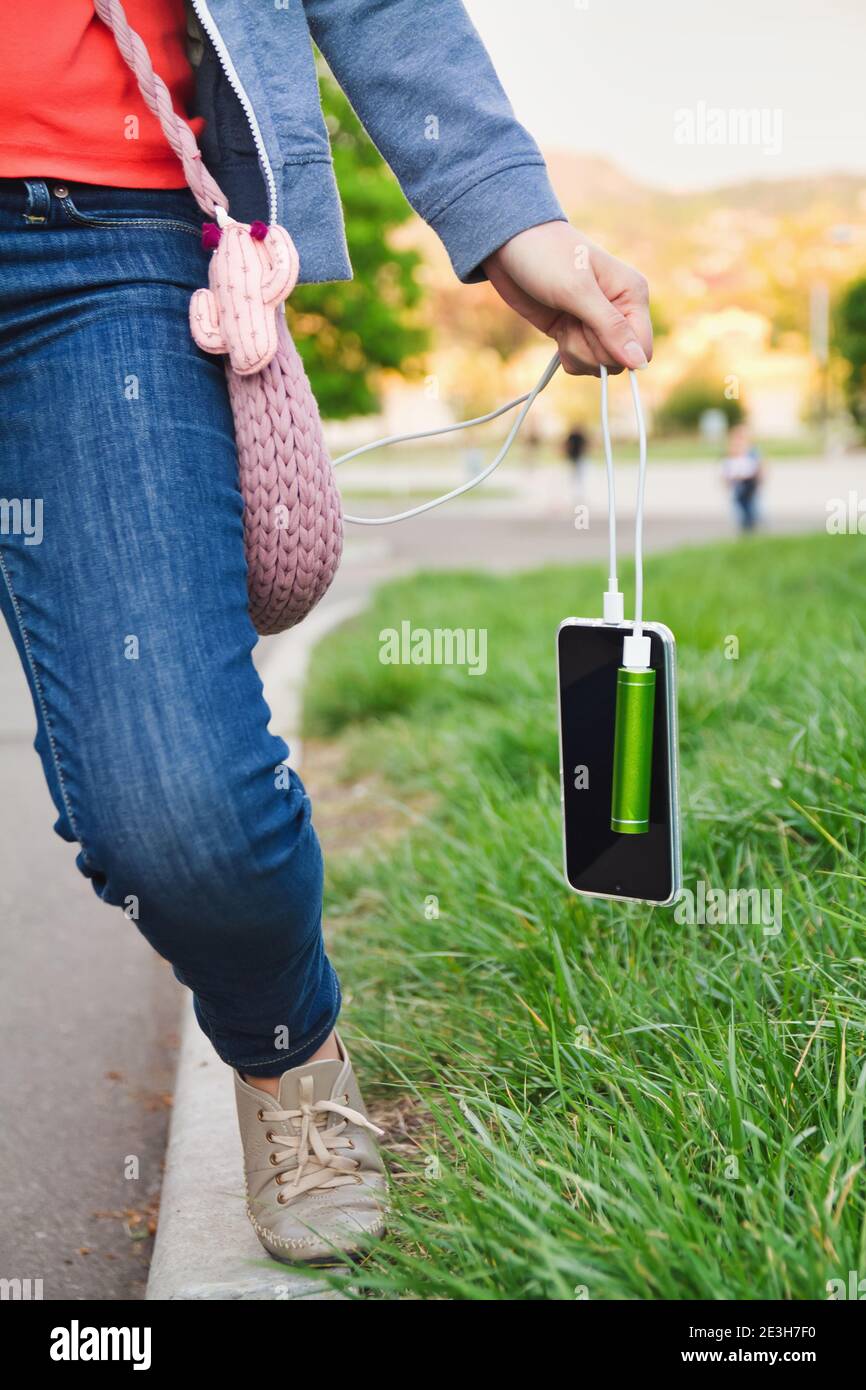 Girl holds by cable a smartphone and an external power bank while ...