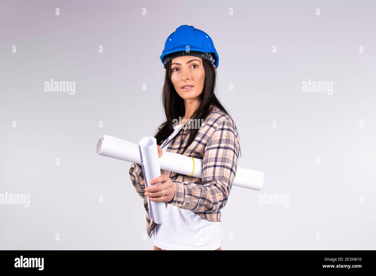Serious woman architect in blue hard hat with blueprints on gray ...