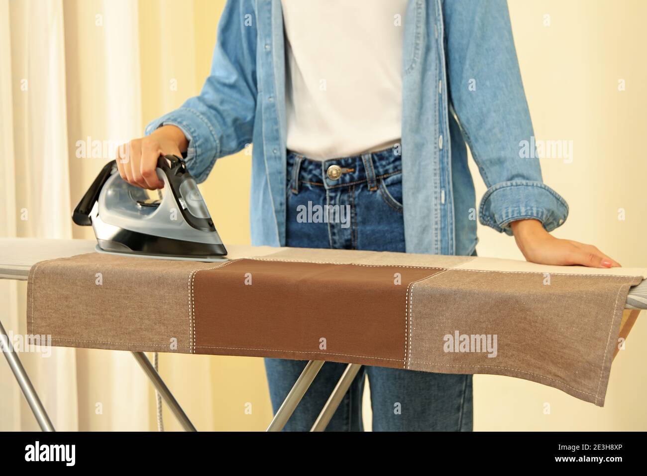 Woman in jeans ironing kitchen towel on ironing board Stock Photo - Alamy