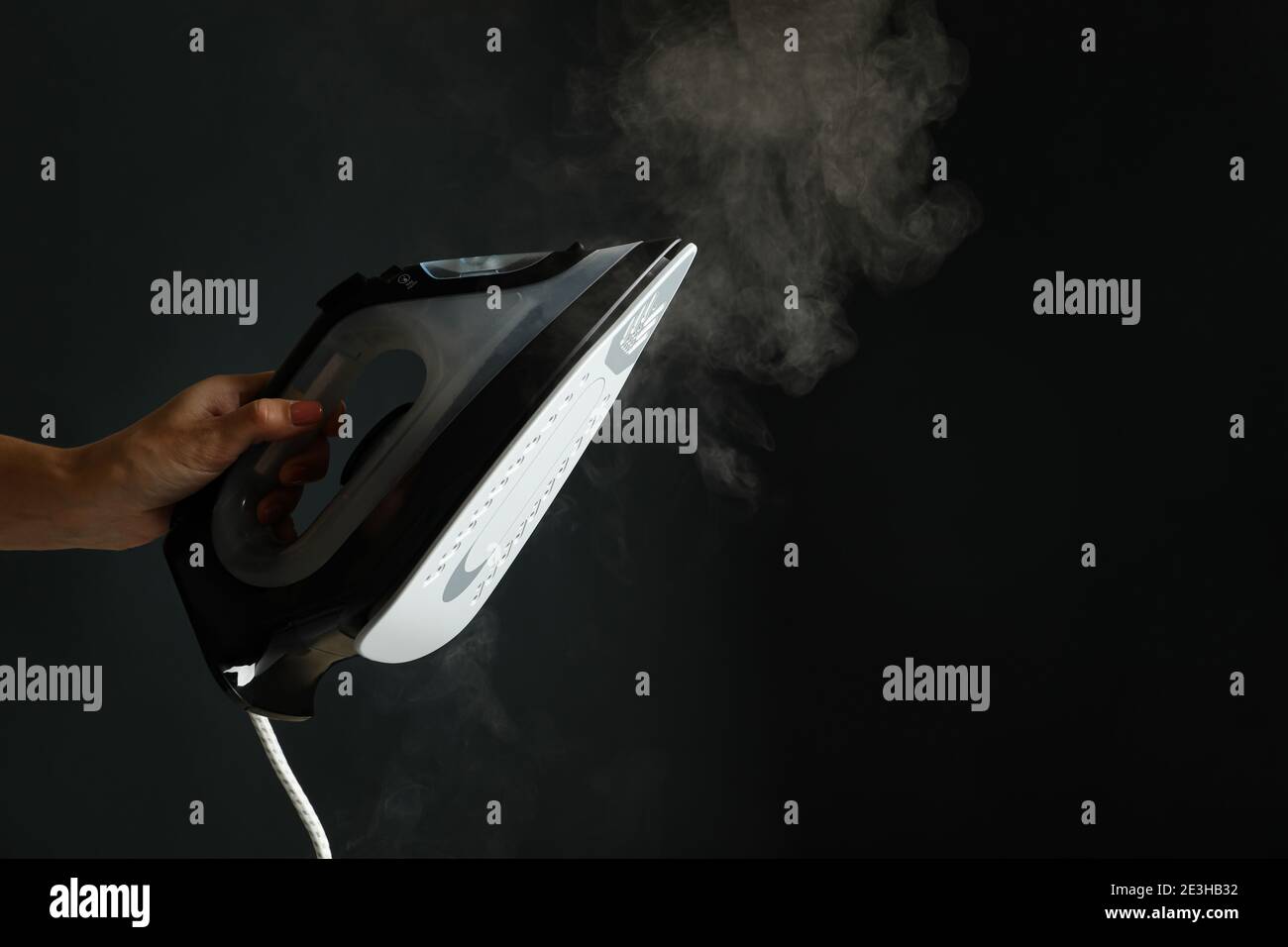 Female hand hold iron on black background Stock Photo - Alamy