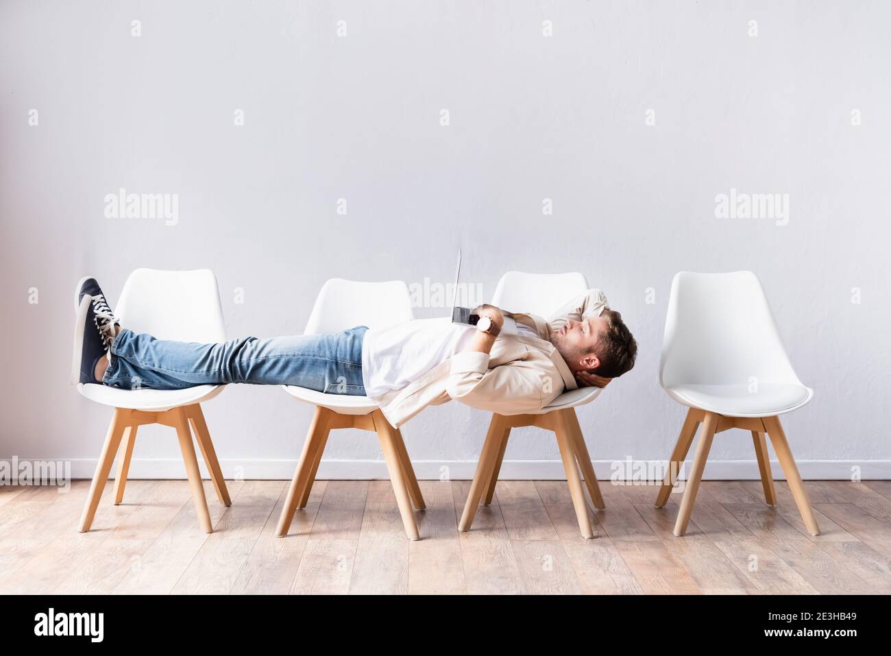 Young freelancer using laptop while lying on chairs in hall Stock Photo ...