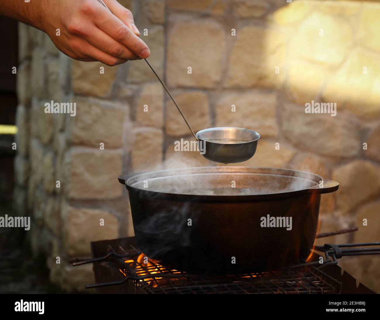 Man holding ladle over metal cauldron with soup on fire Stock Photo - Alamy