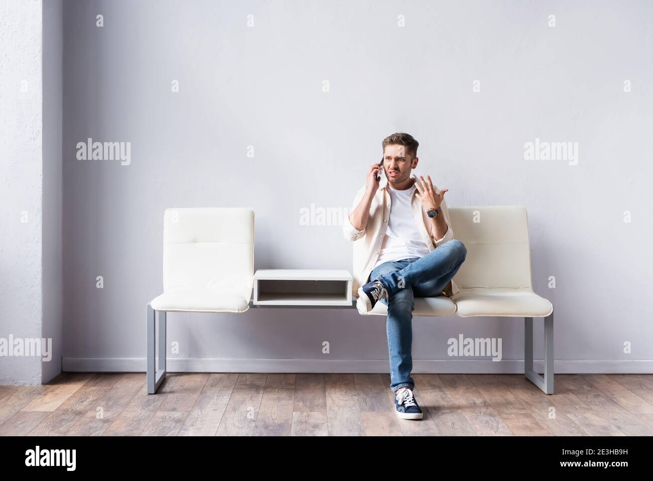 Angry man talking on smartphone while waiting in hall Stock Photo - Alamy