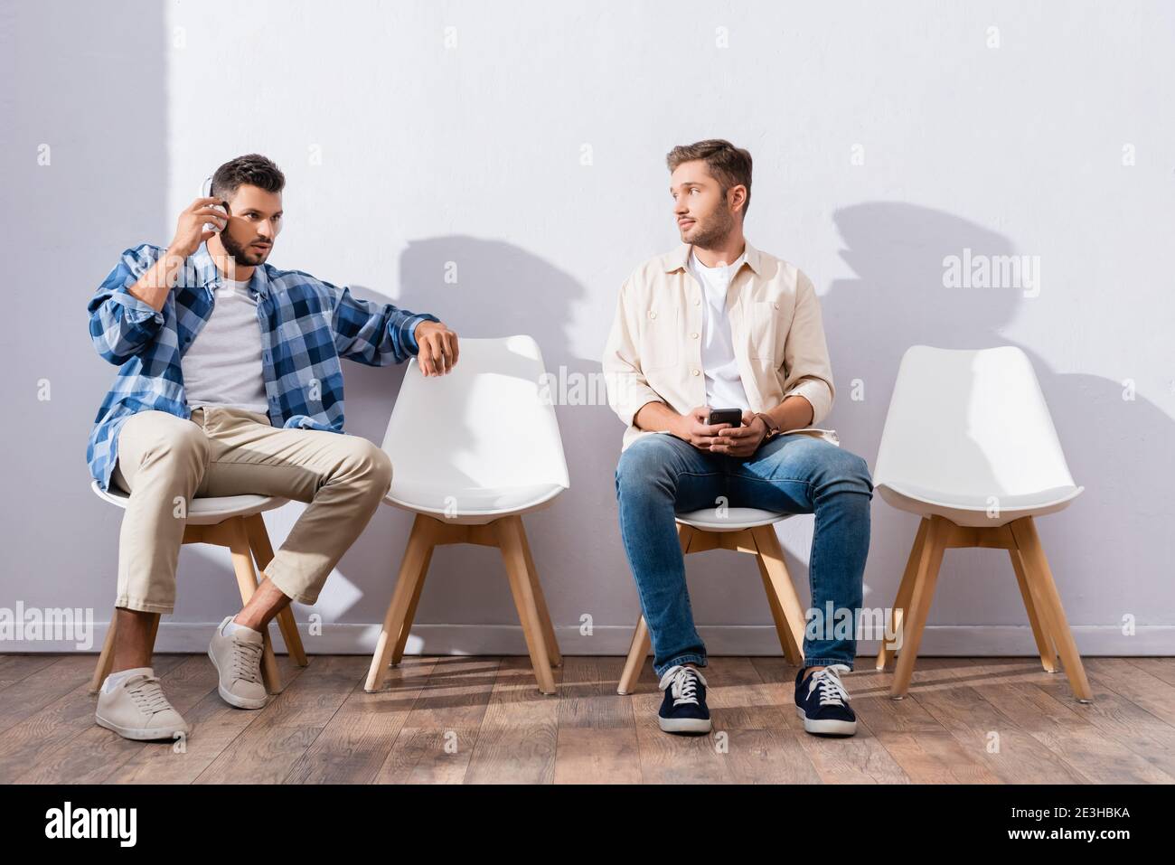 Men with headphones and smartphone sitting on chairs in queue Stock ...