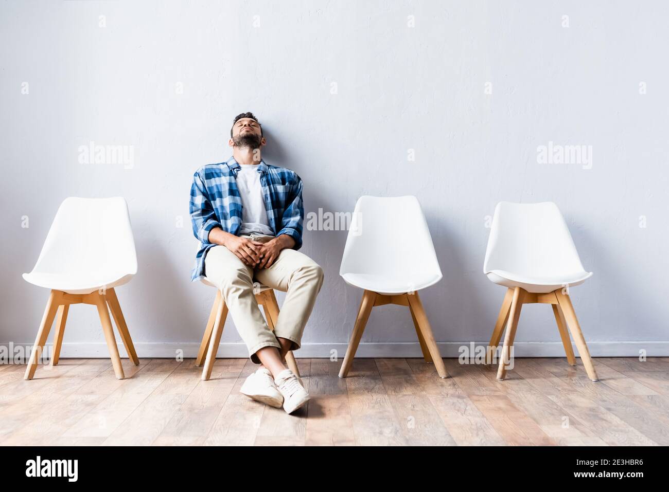 Tired man sitting on chair while waiting in hall Stock Photo - Alamy