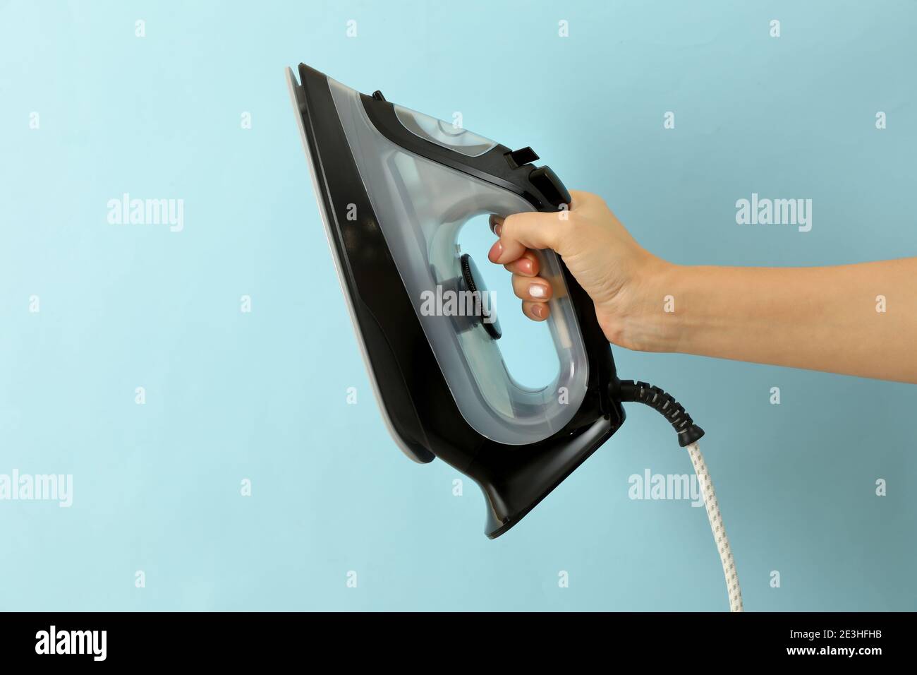 Female hand hold modern iron on blue background Stock Photo - Alamy