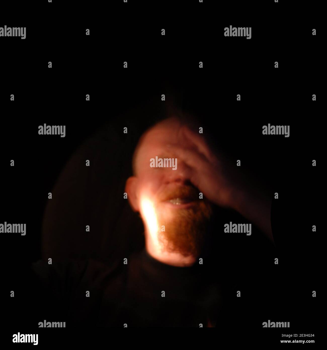 portrait of mans head lit by torchlight against a black background ...