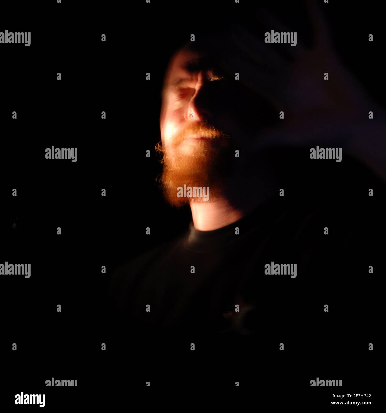 portrait of mans head lit by torchlight against a black background ...