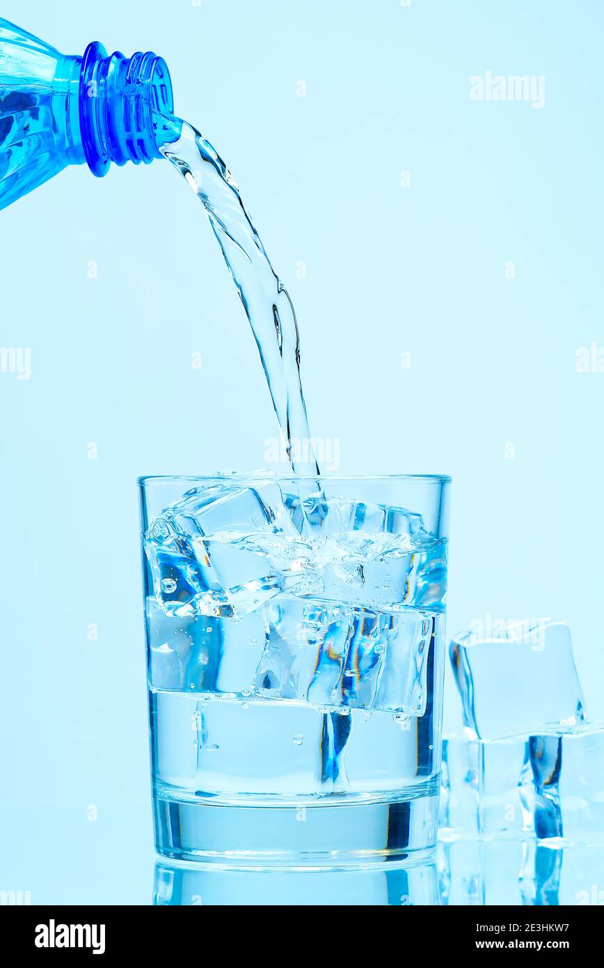 Pouring clean drinking water from blue plastic bottle into glass on ...