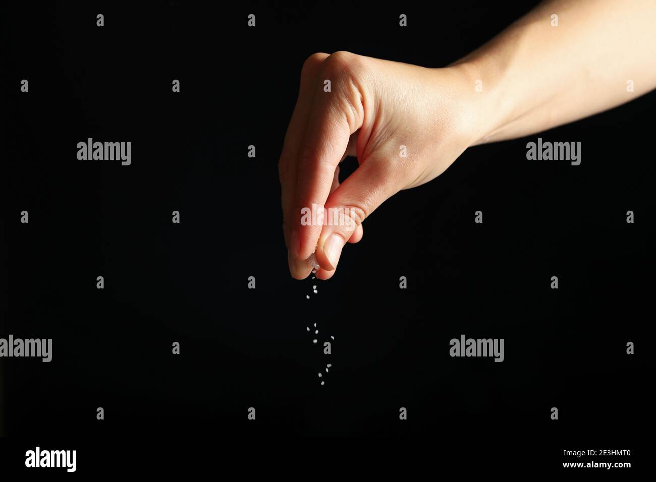 Female hand adding salt on black background Stock Photo - Alamy