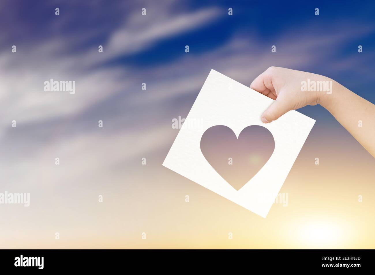 Silhouette of hand is raising paper with shape heart at sunset ...