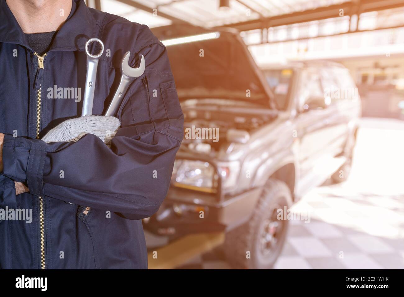 Car repairman wearing a dark blue uniform standing and holding a wrench ...