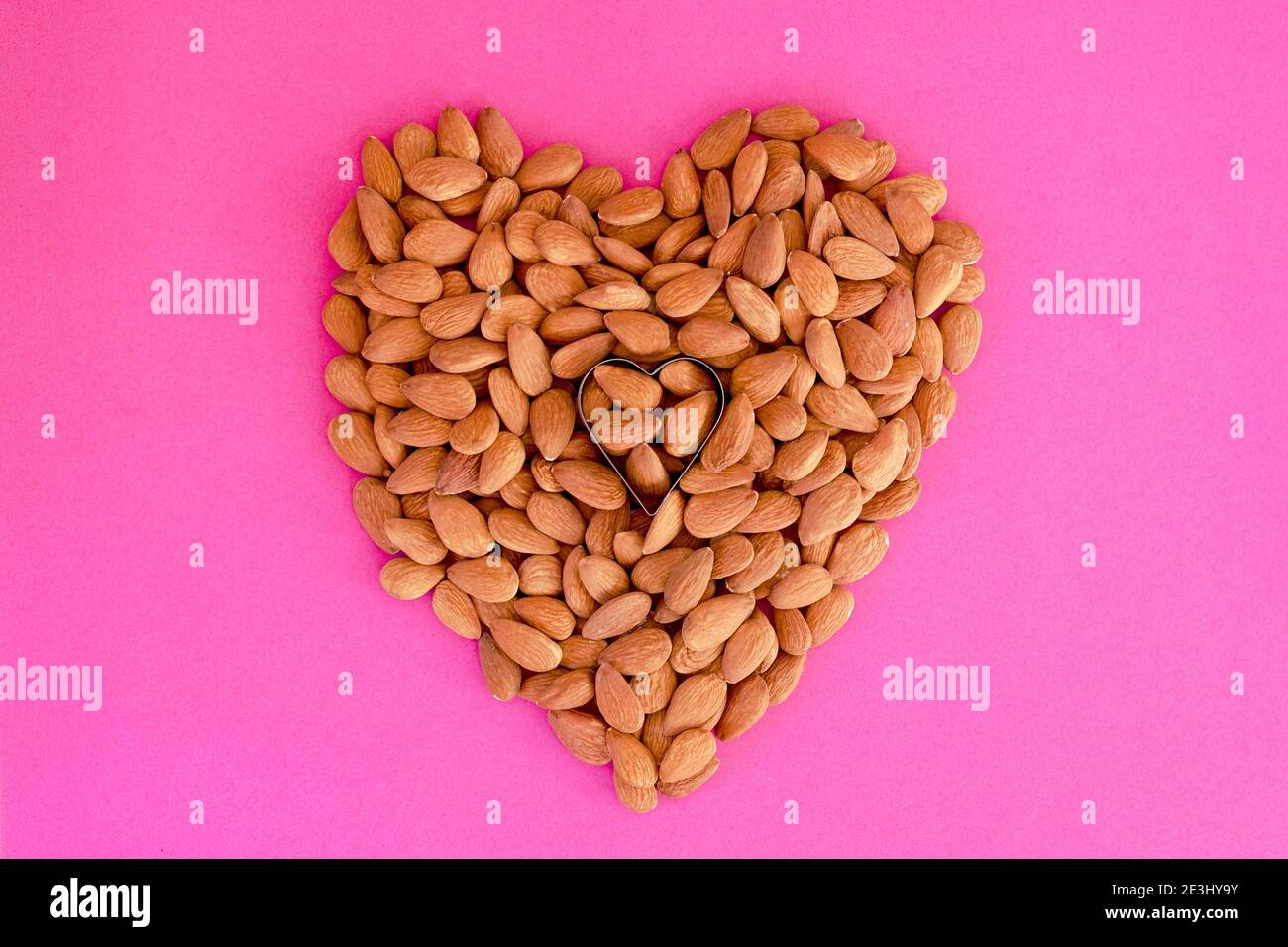 Almonds heap in heart shape on pink background. Isolated. Valentine's ...