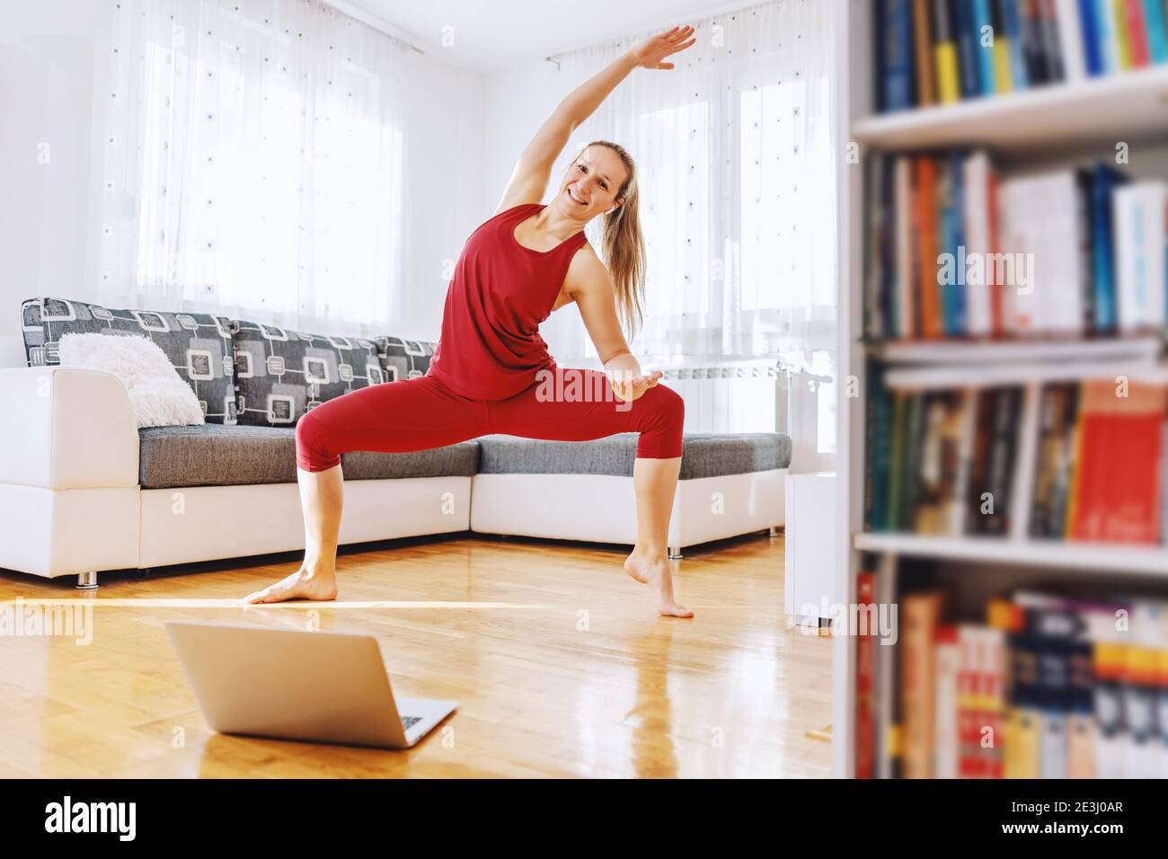 Smiling fit yoga instructor standing in goddess yoga posture and having online class. Home ...