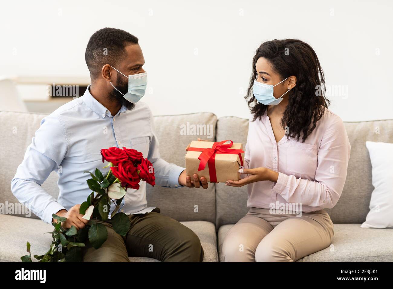 Black man in mask giving roses and box to woman Stock Photo - Alamy