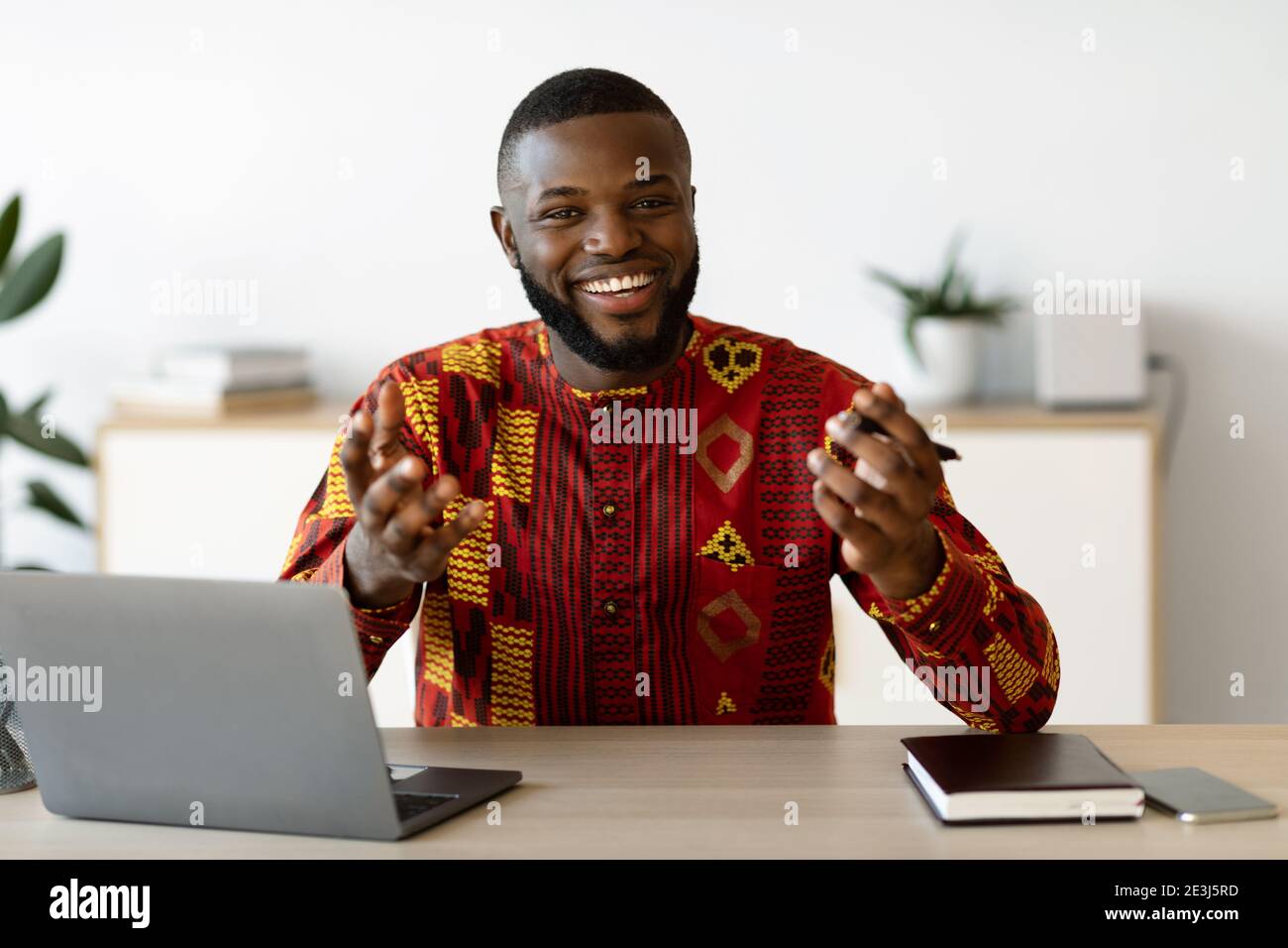 Joyful African Man In Traditional Costume Sitting At Desk Talking At ...