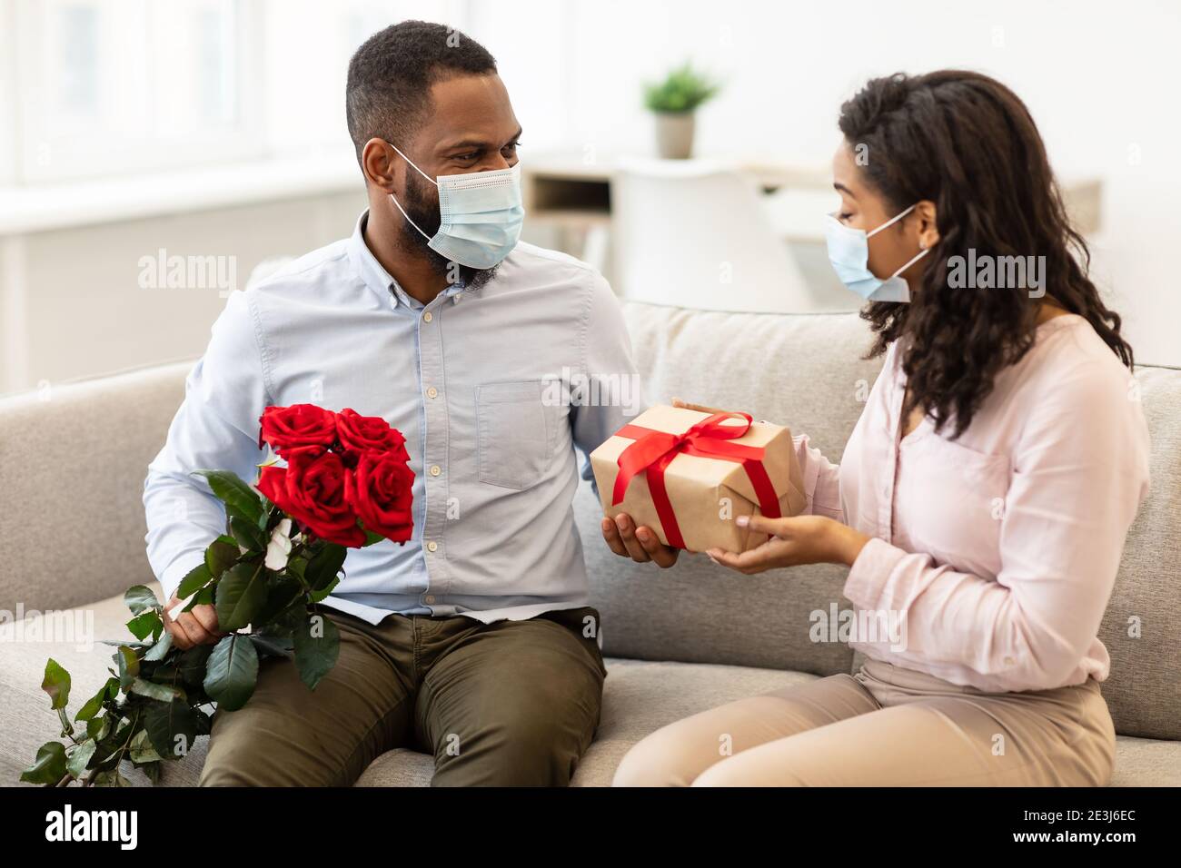 Happy black guy giving red roses and box to woman Stock Photo - Alamy