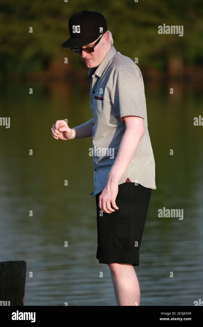 Man looking at something on a pier, with a body of water behind him ...