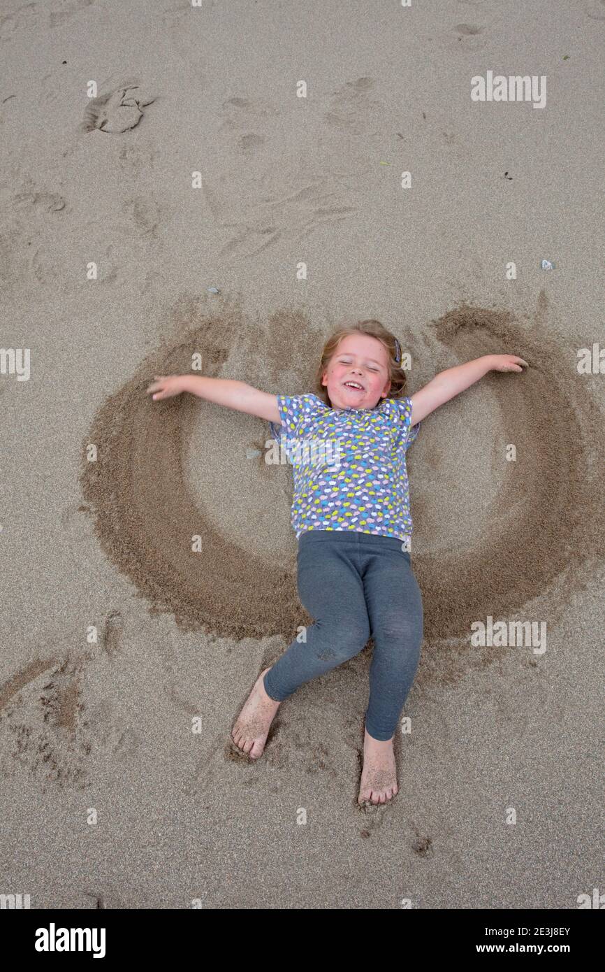 Young girl making sand angels at the beech Stock Photo - Alamy