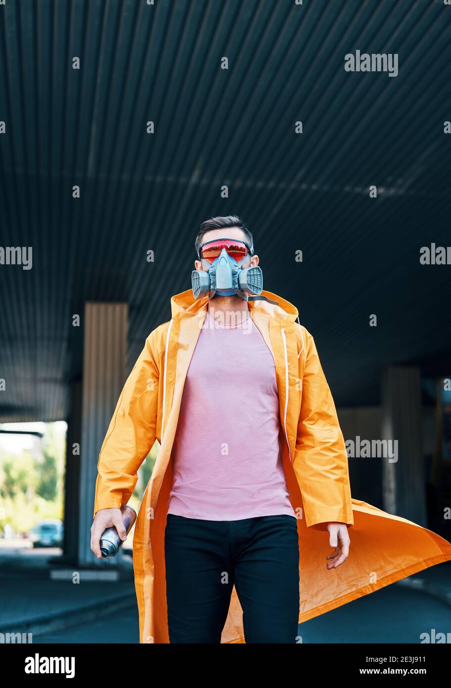 Trendy young man in respirator mask walking down the street looking at ...