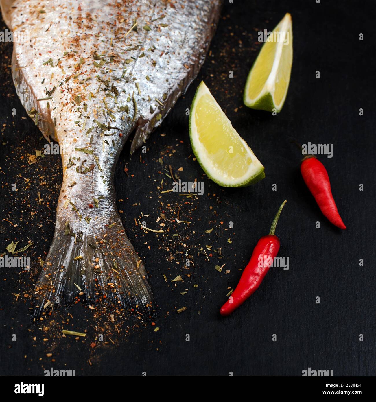 Tail of fresh raw dorado on black slate stone board with spices, herbs ...