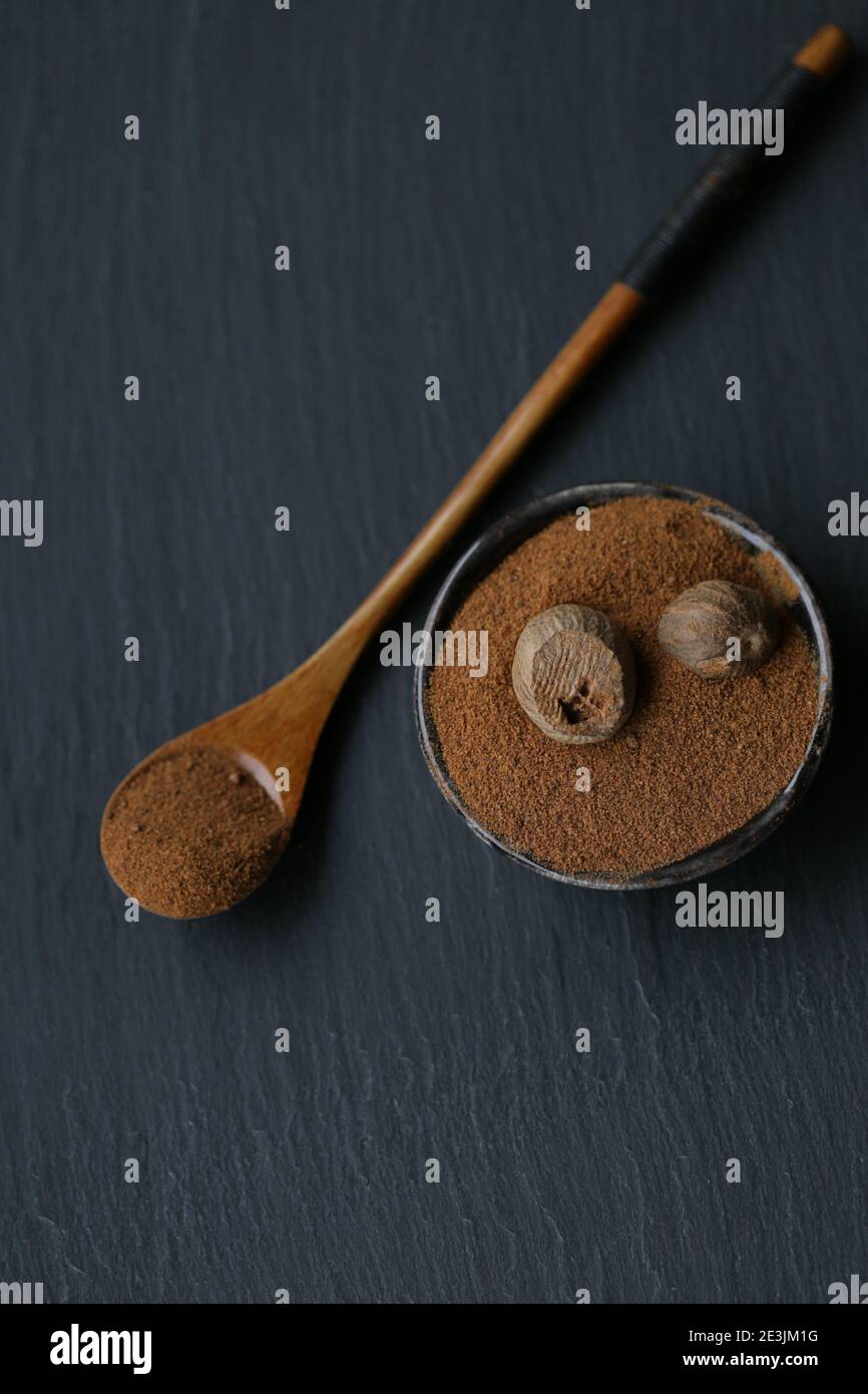 Nutmeg.Whole and grated nutmeg in a black cup and wooden spoon on a ...
