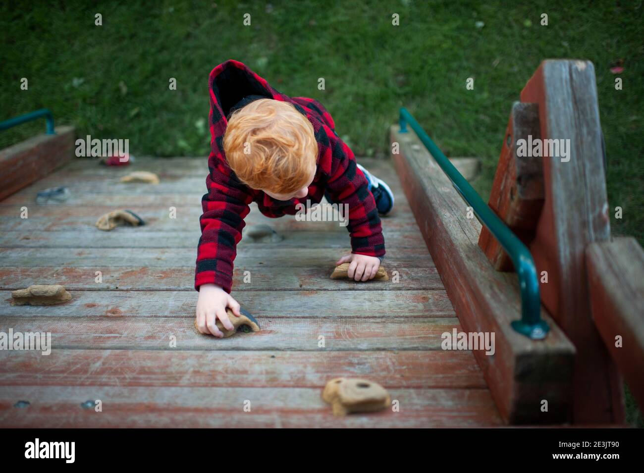 Birds eye view of toddler climbing rock wall on playset in fall coat ...